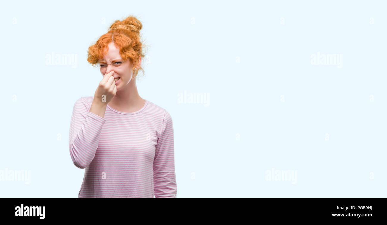 Young redhead woman smelling something stinky and disgusting ...