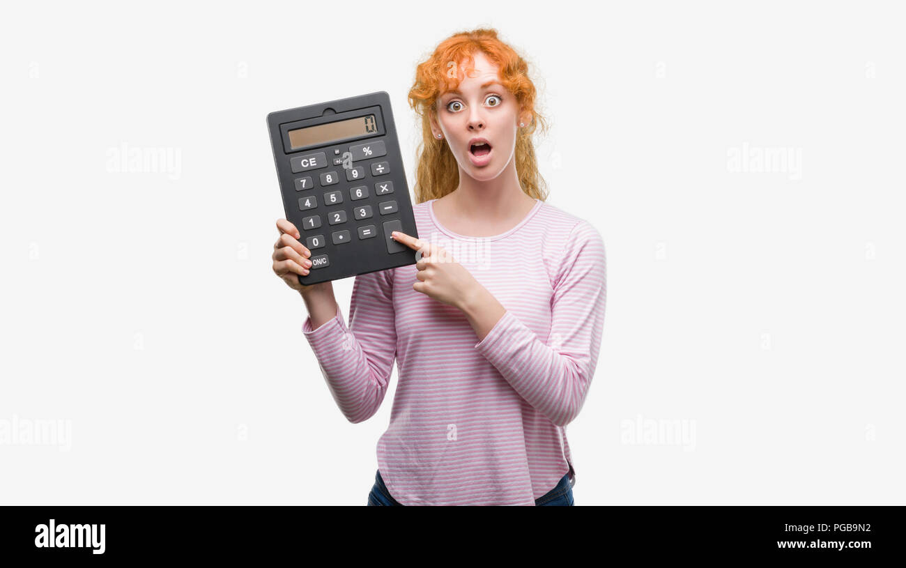 Young redhead woman holding big calculator scared in shock with a ...