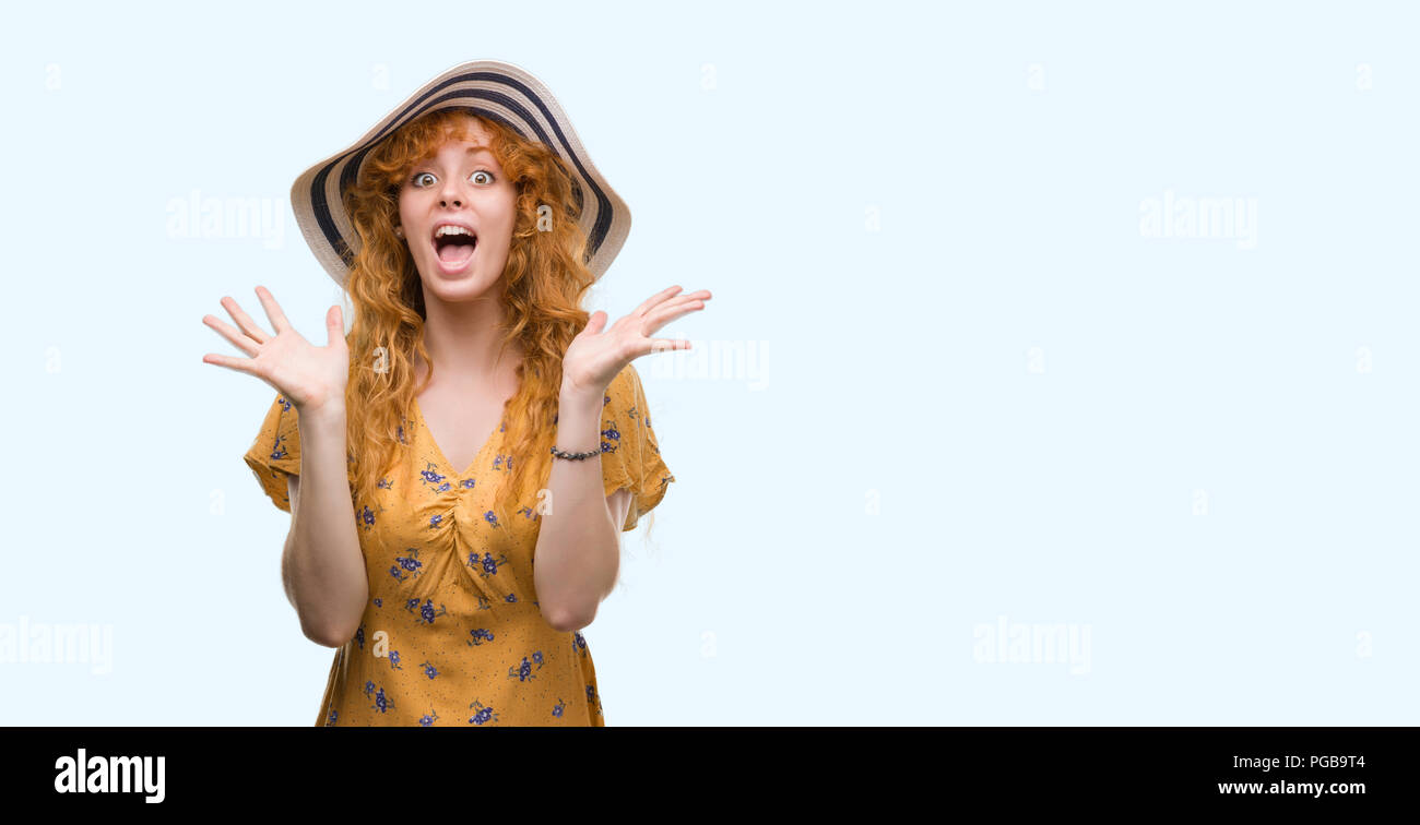 Young redhead woman wearing summer hat and dress very happy and excited ...