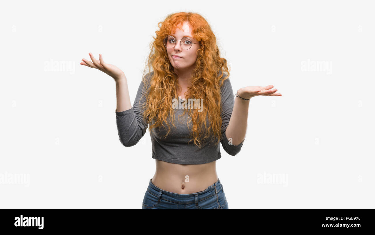 Young redhead woman clueless and confused expression with arms and ...