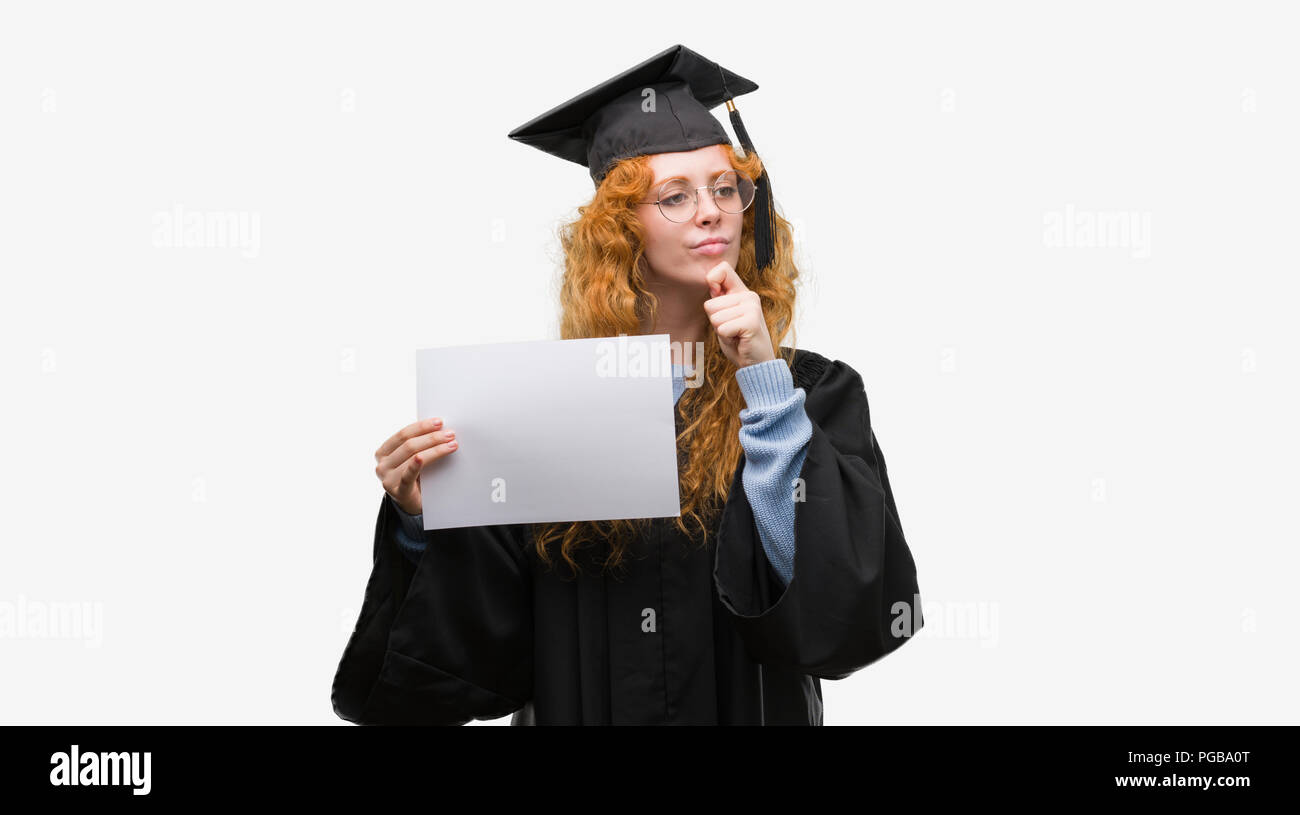 Young redhead woman wearing graduate uniform holding degree serious ...