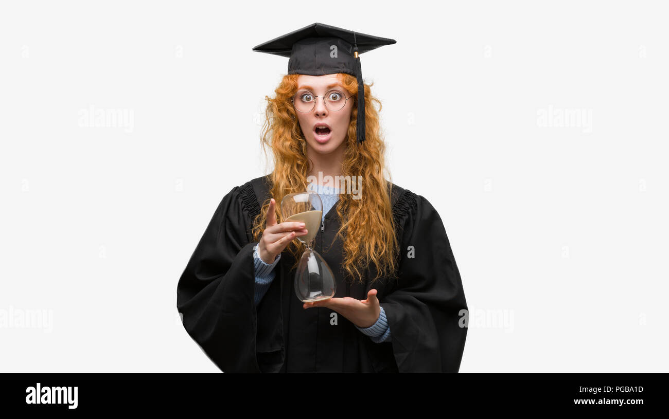 Young redhead student woman wearing graduated uniform holding hourglass ...