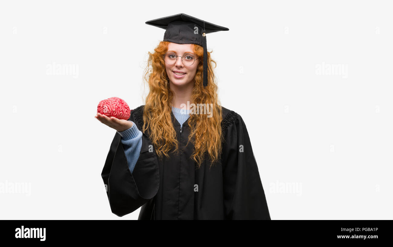Young redhead student woman wearing graduated uniform holding brain ...