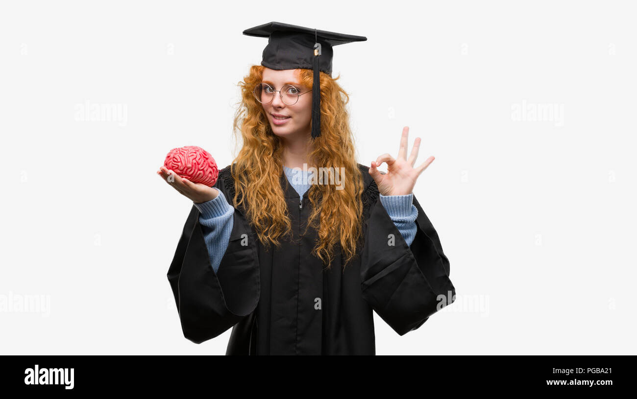 Young redhead student woman wearing graduated uniform holding brain ...