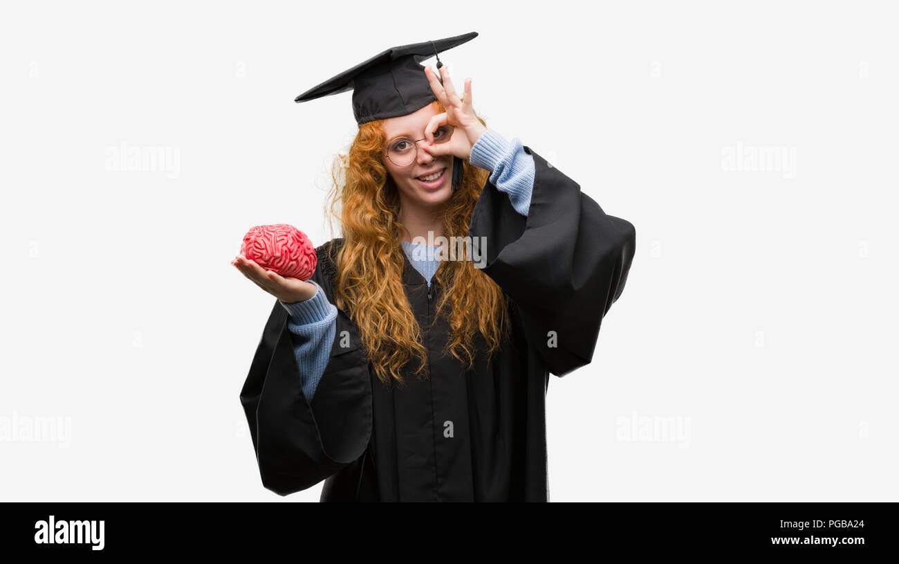 Young redhead student woman wearing graduated uniform holding brain ...