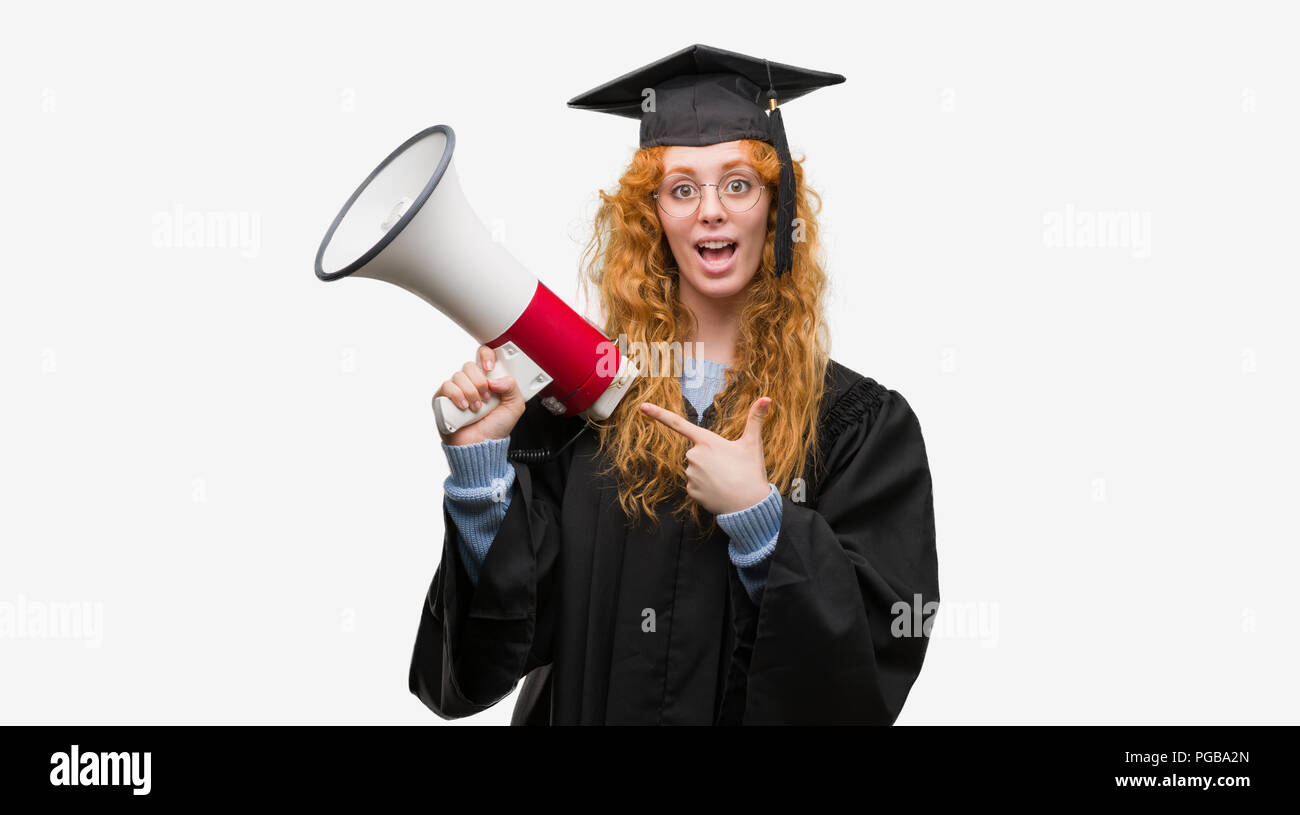 Young redhead student woman wearing graduated uniform holding megaphone ...