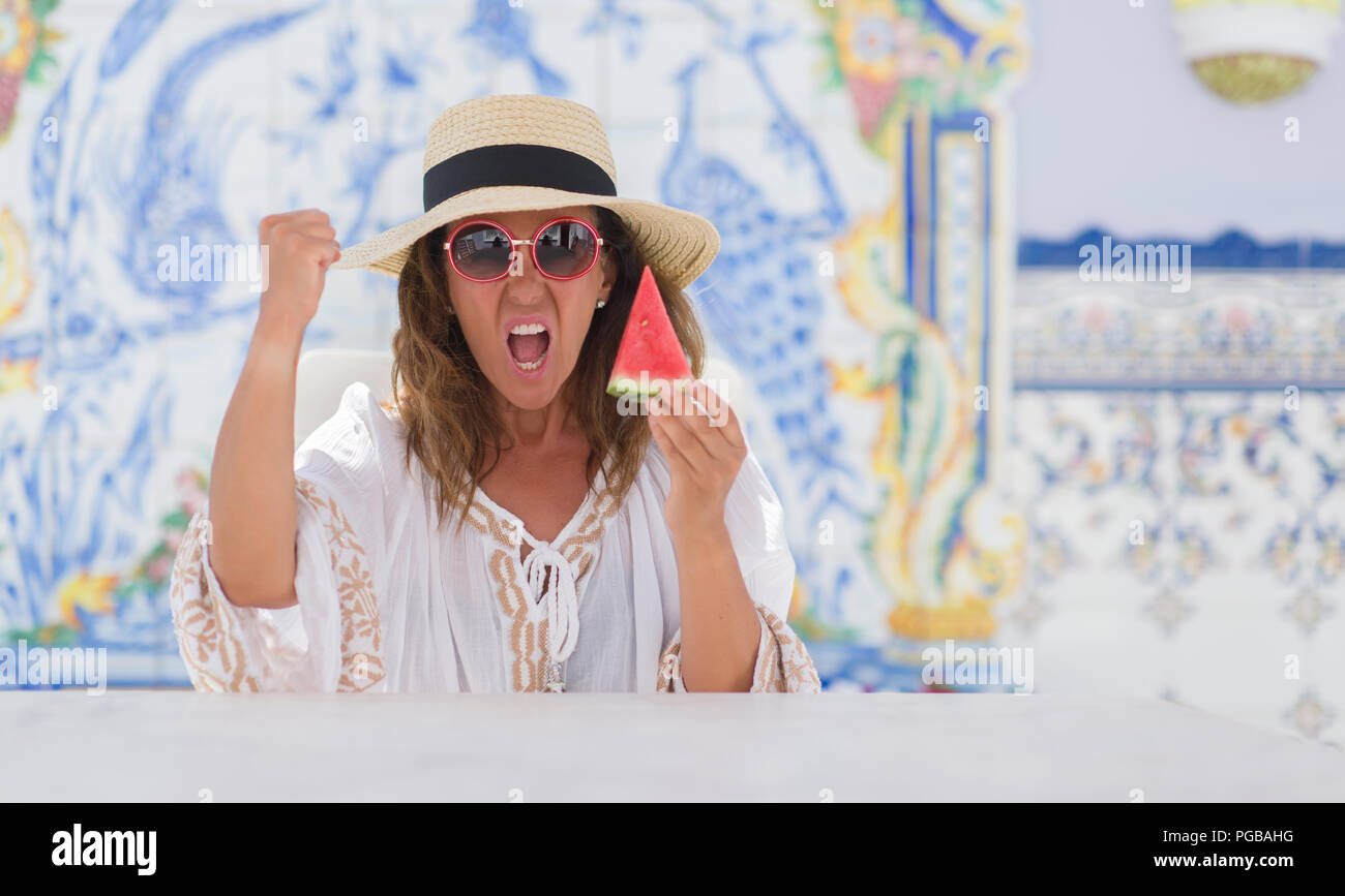 Middle age brunette woman sitting at the table eating watermelon ...