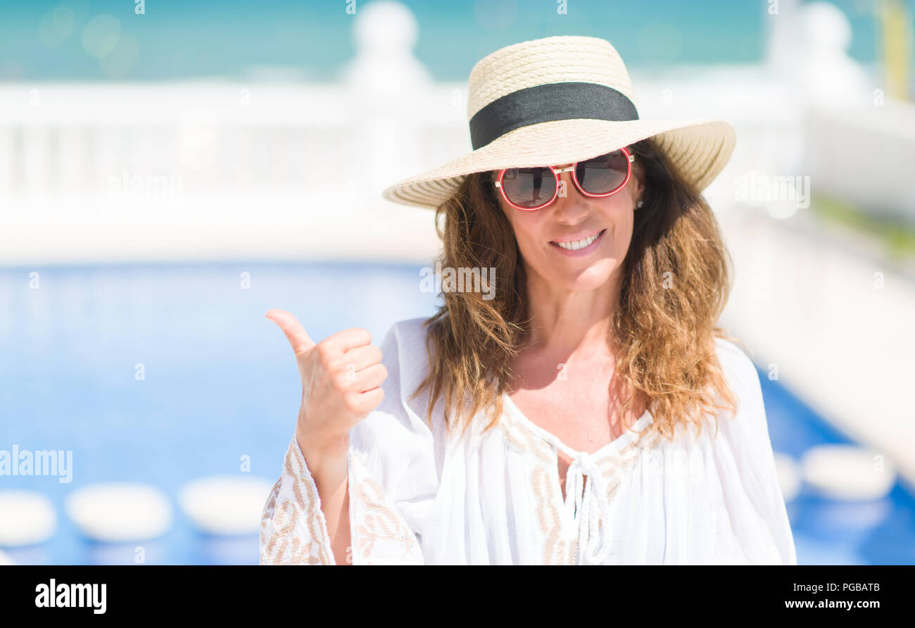 Middle age brunette woman by the swiming pool pointing and showing with ...