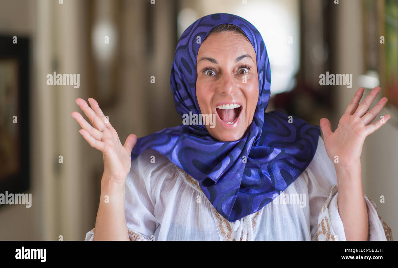 Middle age brunette arabian woman wearing colorful hijab very happy and excited, winner ...