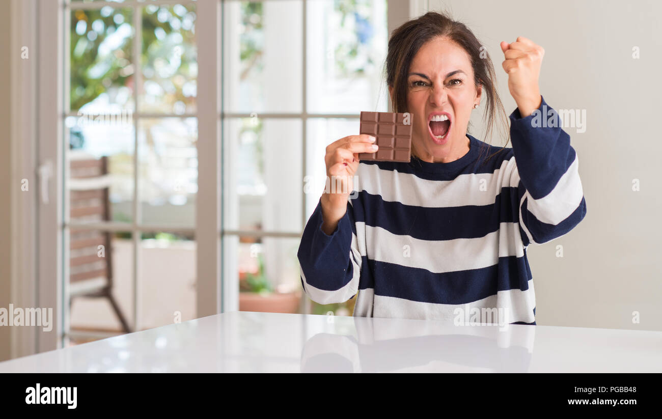 Middle aged woman eating chocolate bar annoyed and frustrated shouting ...