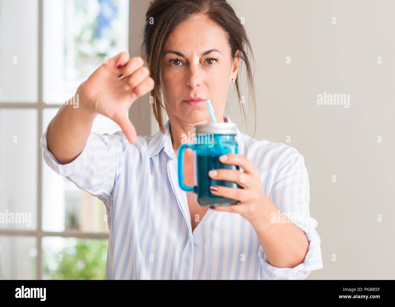 Middle aged woman drinking milk shake in a glass with angry face ...