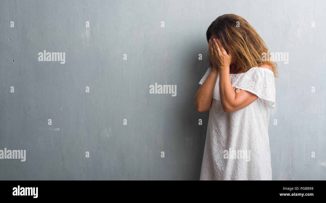 Middle age hispanic woman standing over grey grunge wall with sad ...