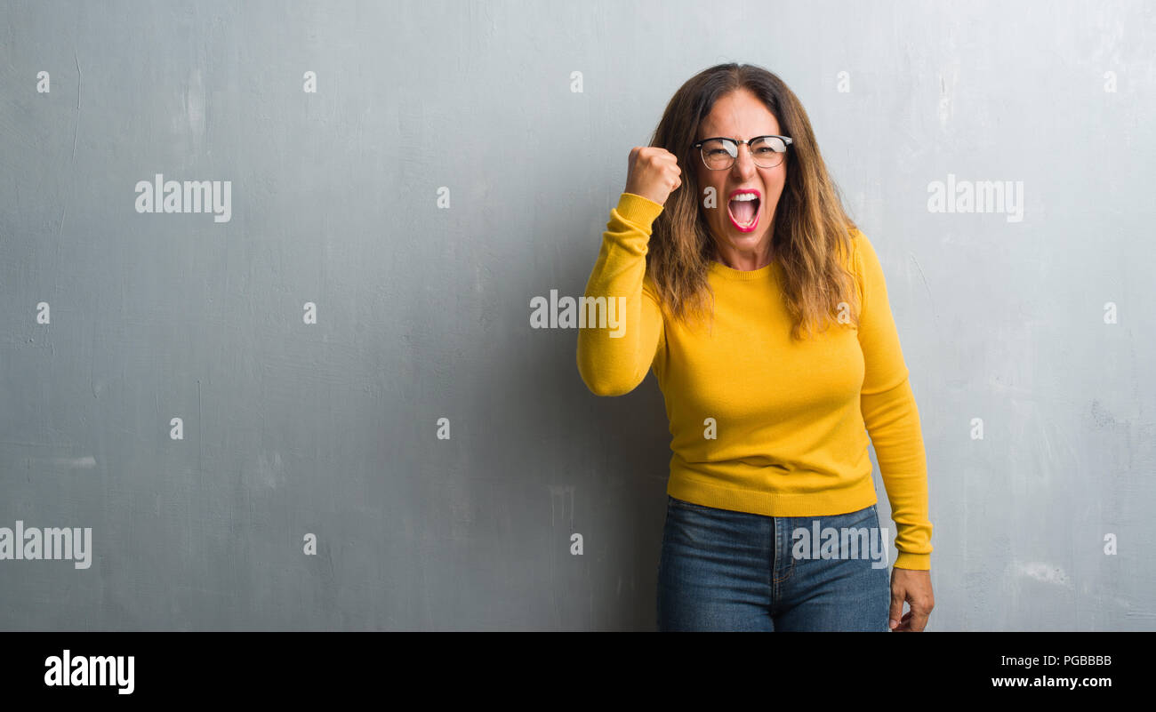 Middle age hispanic woman over grey wall wearing glasses angry and mad ...