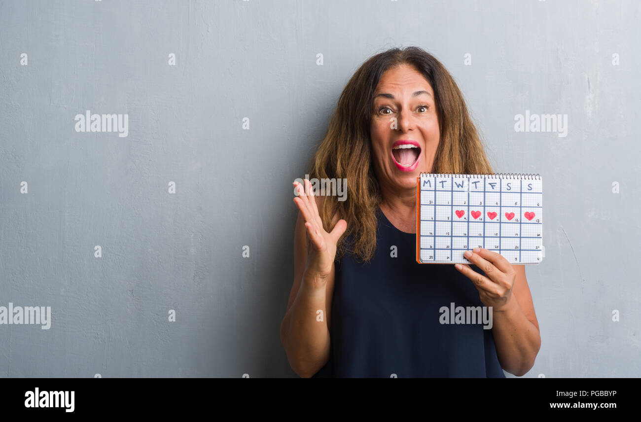 Middle age hispanic woman standing over grey grunge wall holding period ...