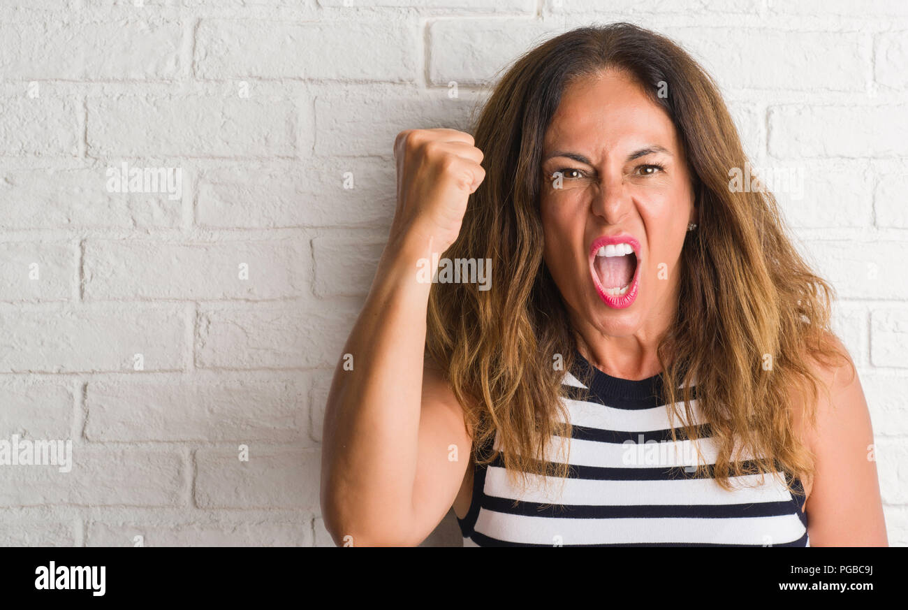 Middle age hispanic woman over white brick wall annoyed and frustrated ...