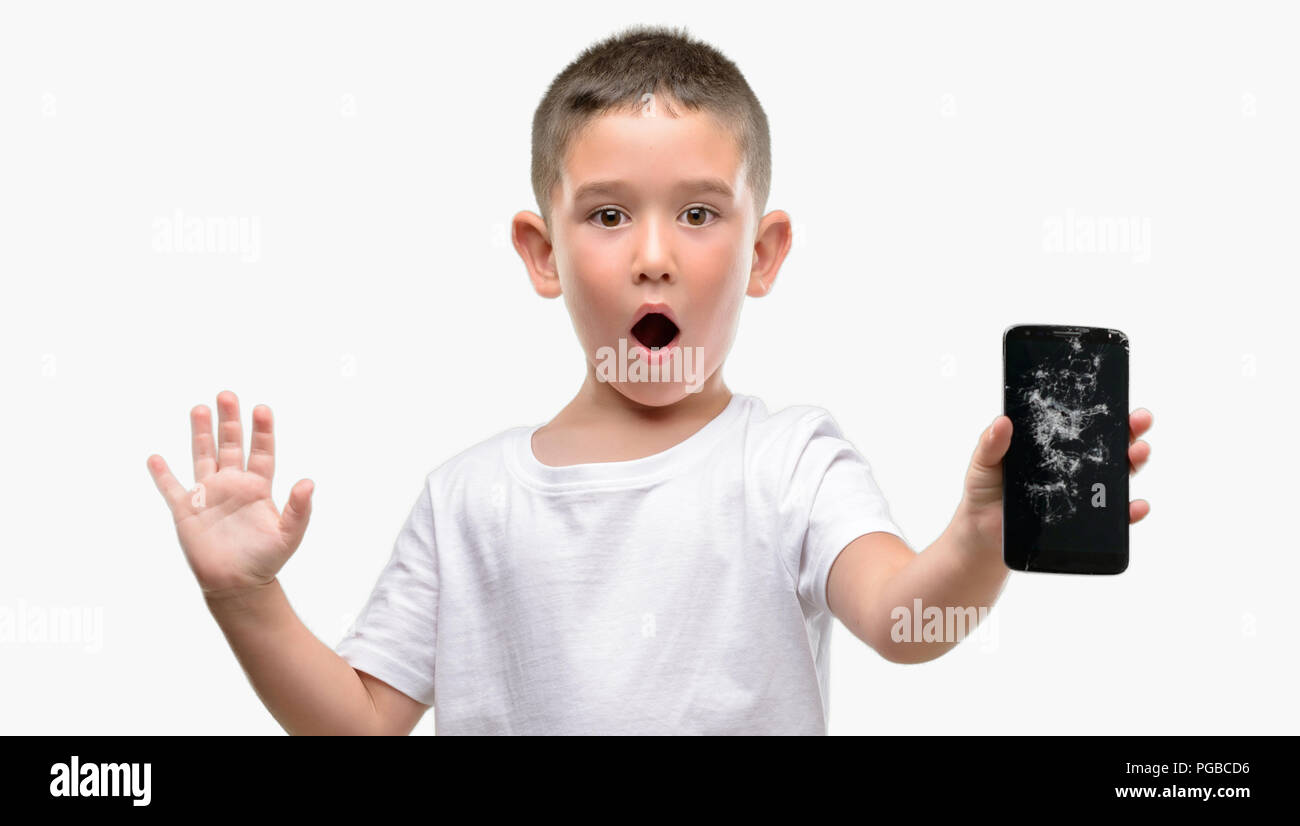Dark haired little child holding broken smartphone scared in shock with ...