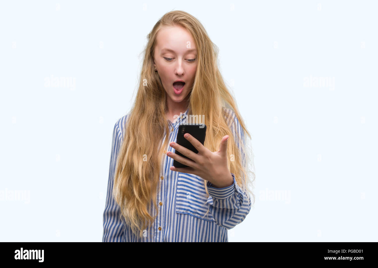 Blonde teenager woman using smartphone scared in shock with a surprise ...