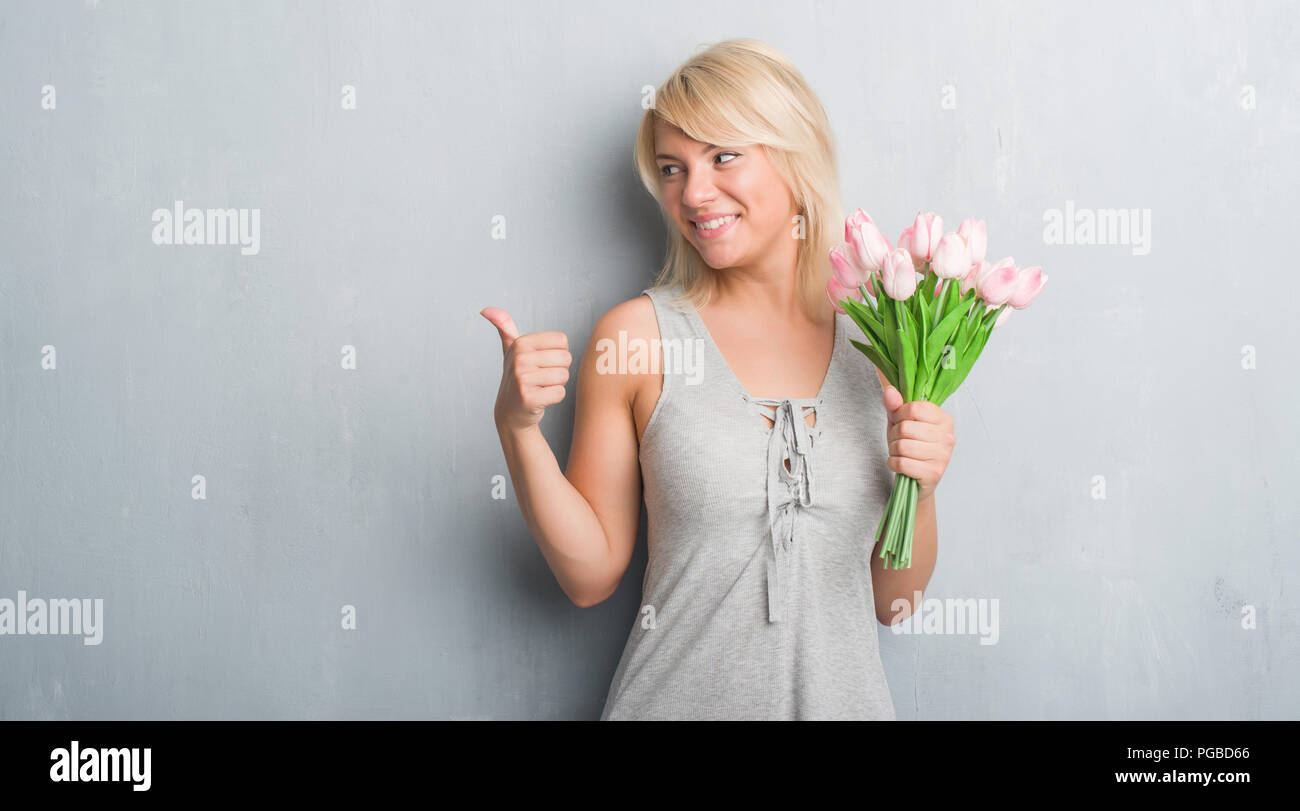 Caucasian adult woman over grey grunge wall holding pink flowers ...