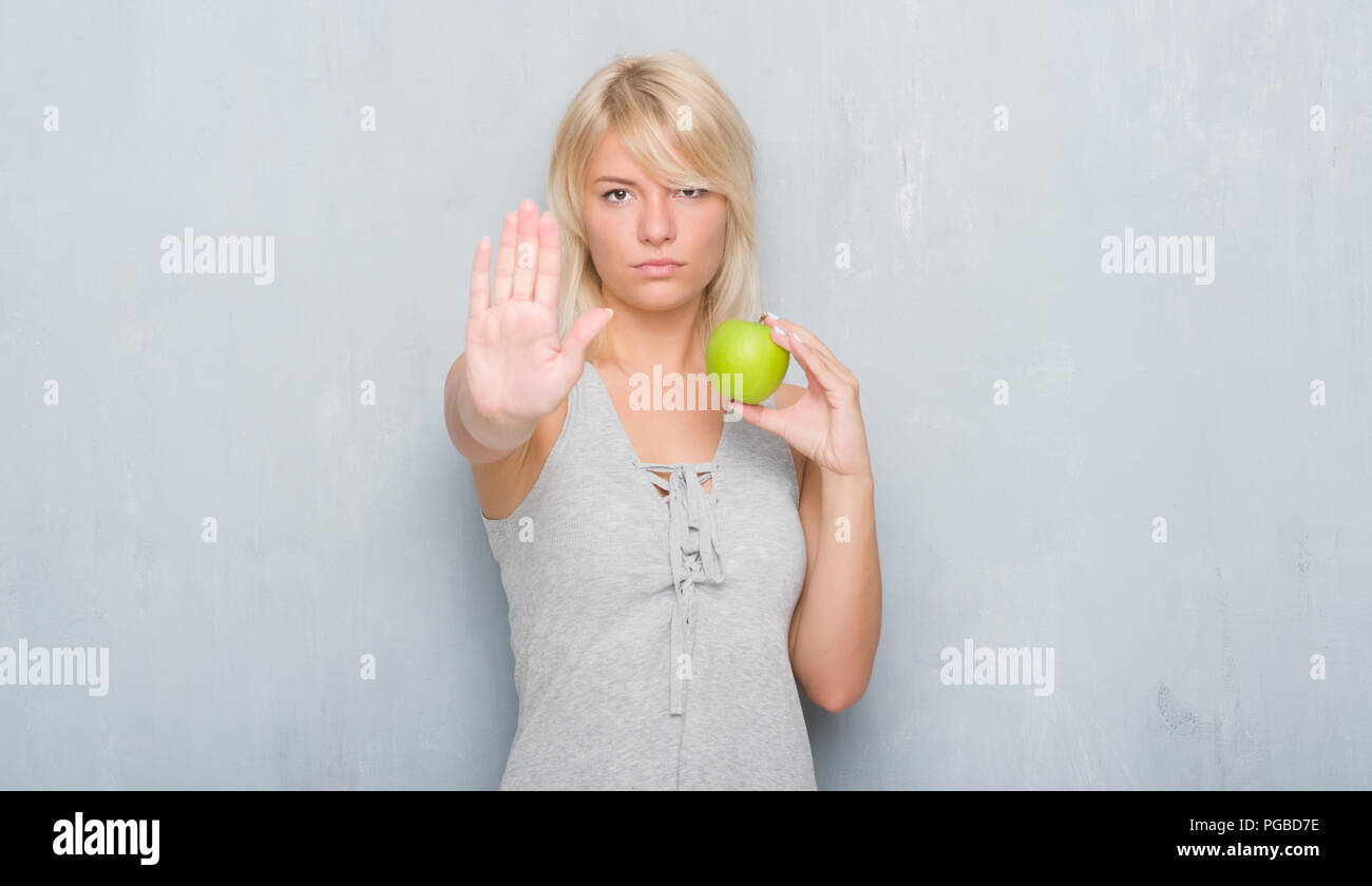 Adult caucasian woman over grunge grey wall eating green apple with ...