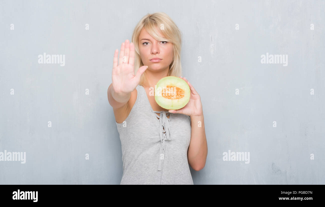 Adult caucasian woman over grunge grey wall eating cantaloupe melon ...