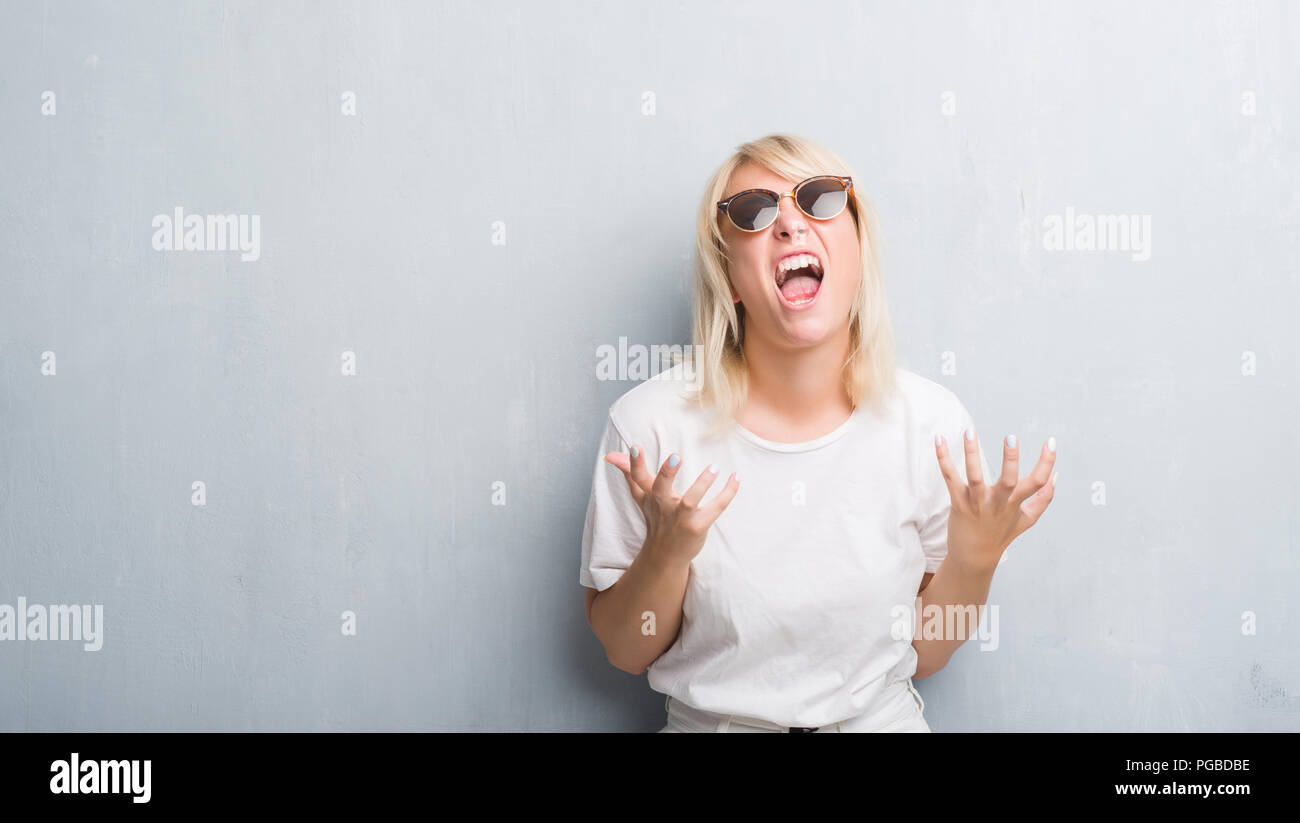 Adult caucasian woman over grunge grey wall wearing sunglasses crazy ...