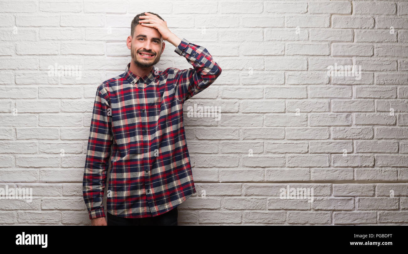 Young adult man over white brick wall stressed with hand on head ...