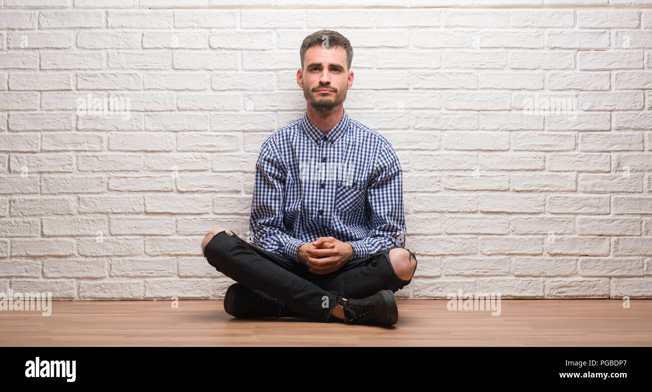 Young adult man sitting over white brick wall depressed and worry for ...