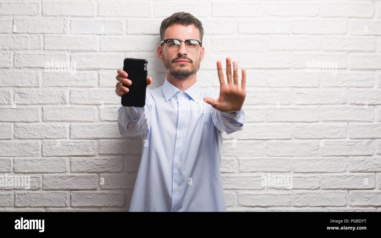 Young adult man talking on the phone standing over white brick wall ...