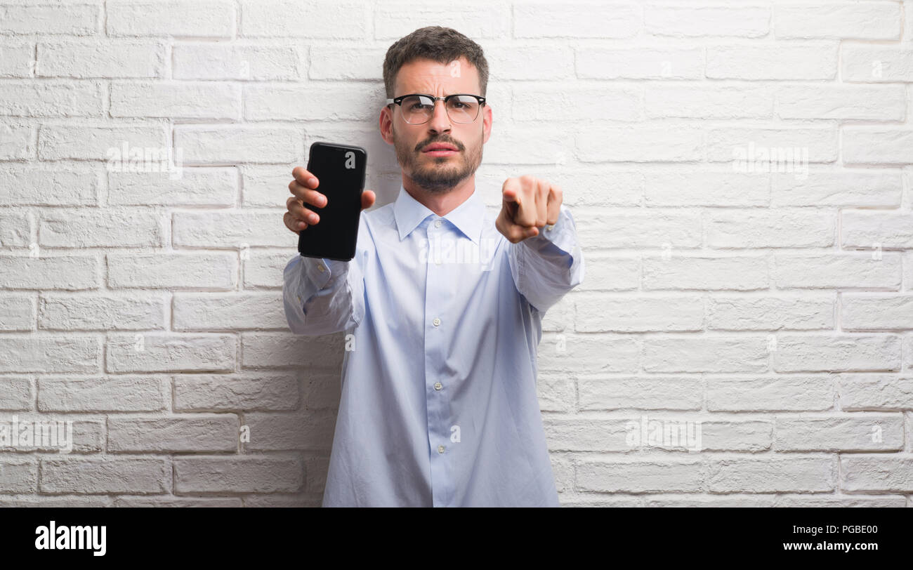 Young adult man talking on the phone standing over white brick wall ...