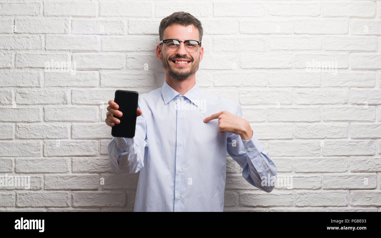 Young adult man talking on the phone standing over white brick wall ...