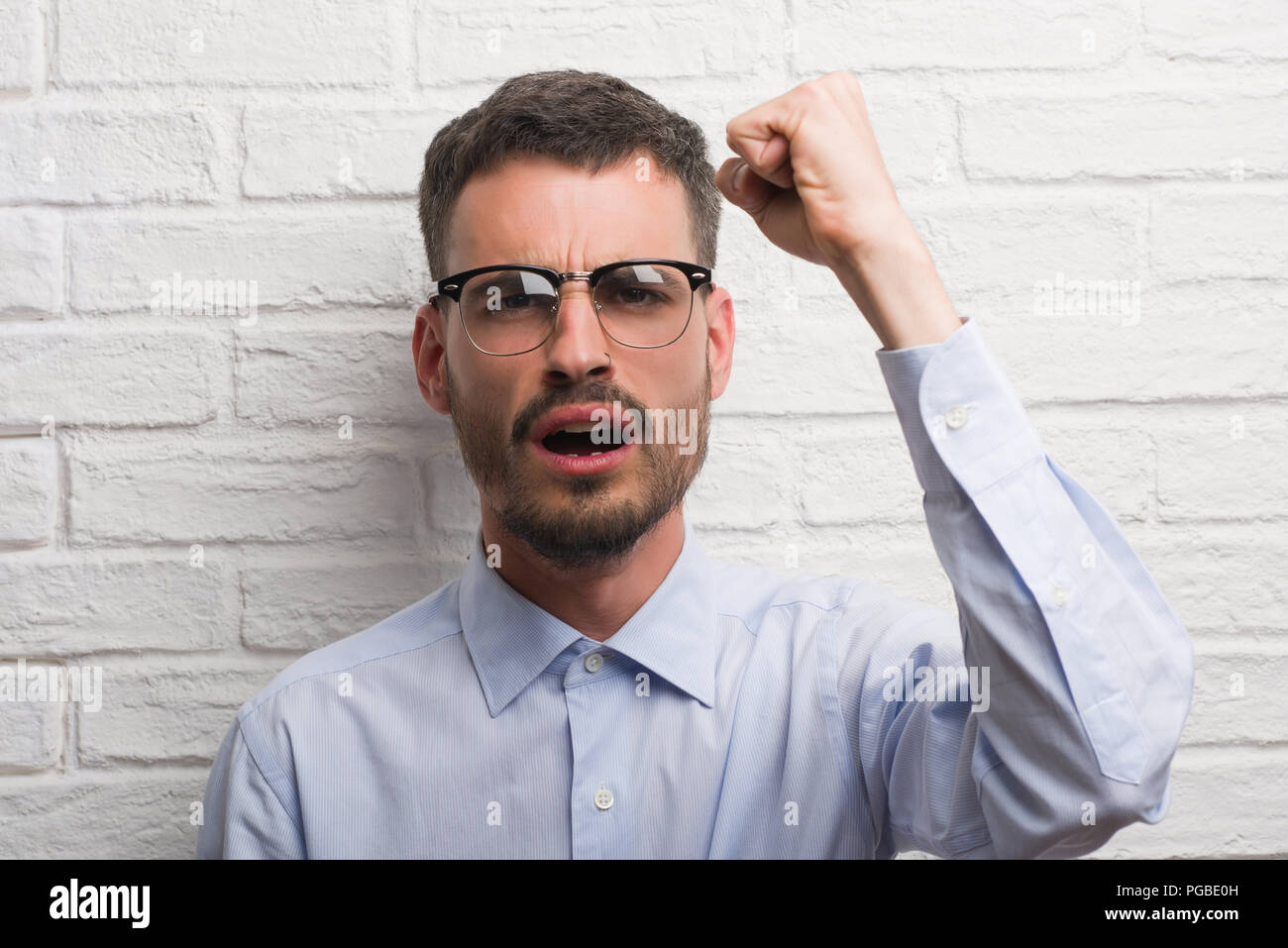 Young adult business man standing over white brick wall annoyed and ...