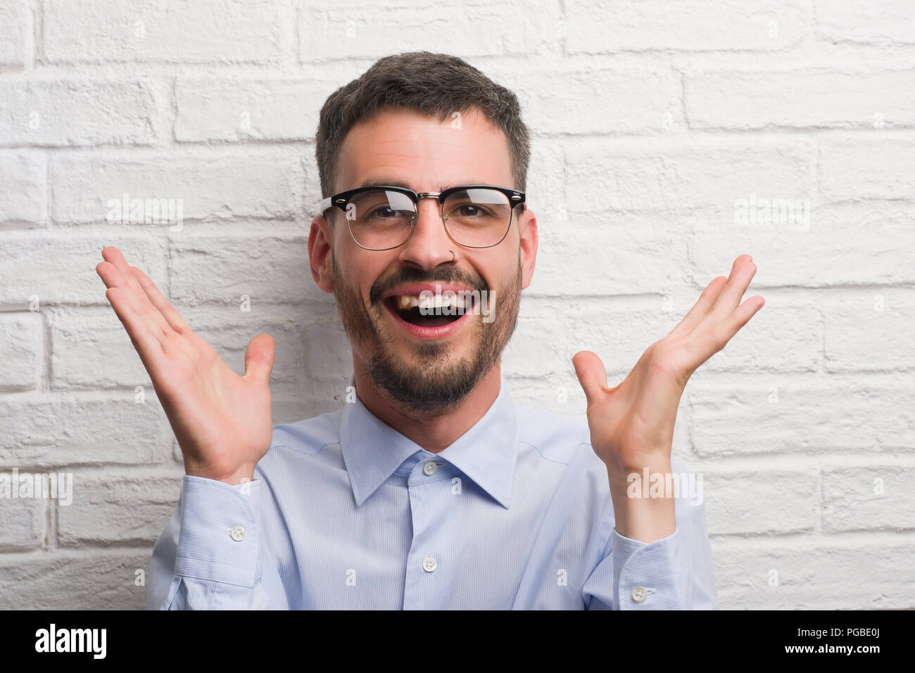 Young adult business man standing over white brick wall very happy and ...