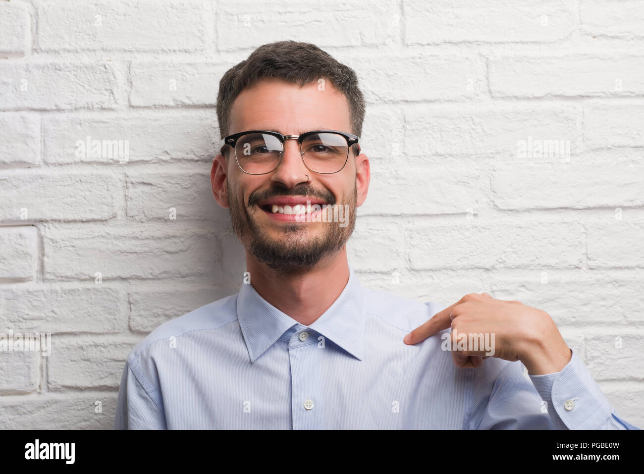 Young adult business man standing over white brick wall with surprise ...