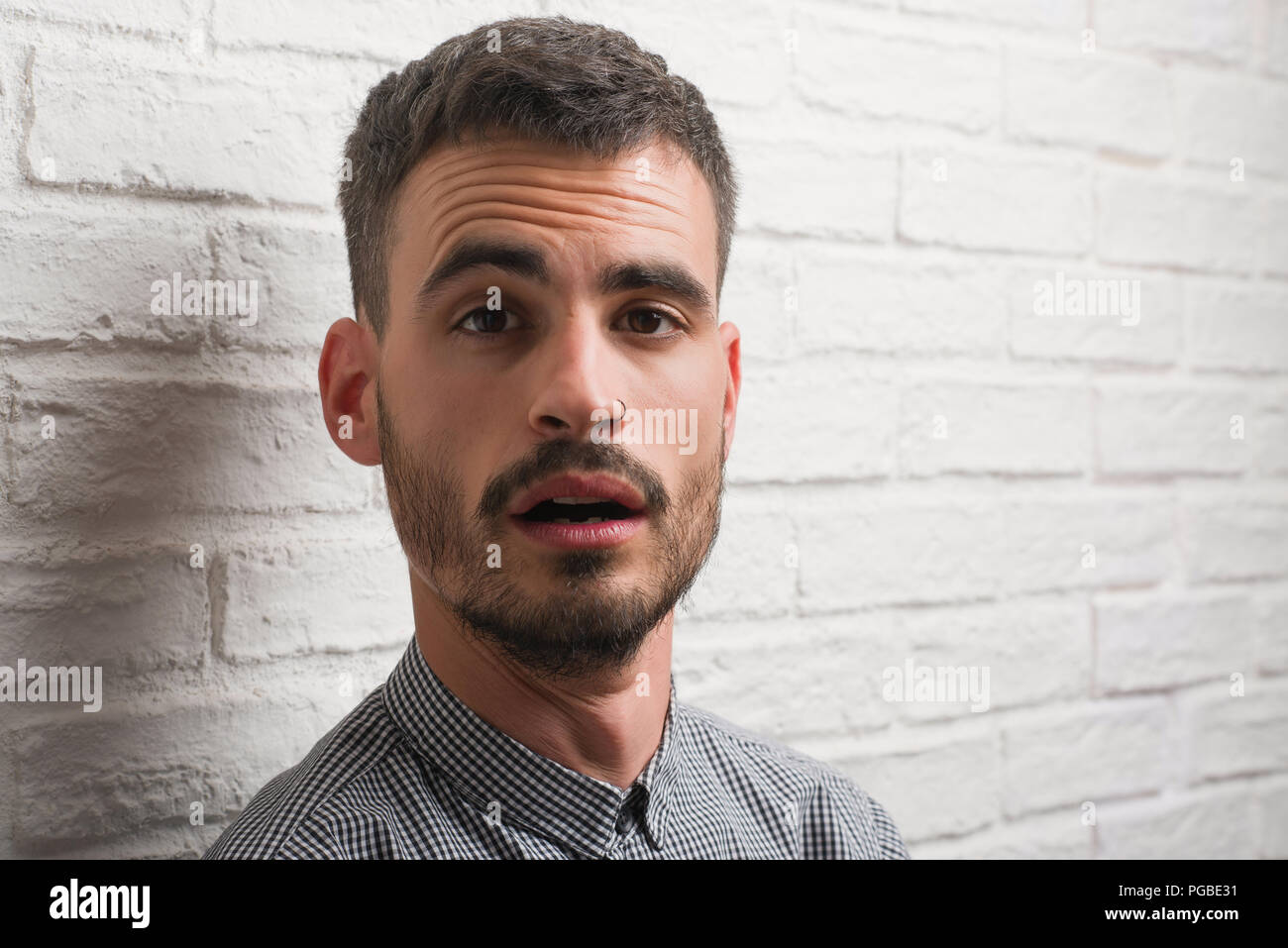Young adult man standing over white brick wall scared in shock with a ...