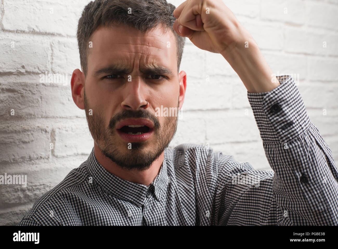 Young adult man standing over white brick wall annoyed and frustrated ...