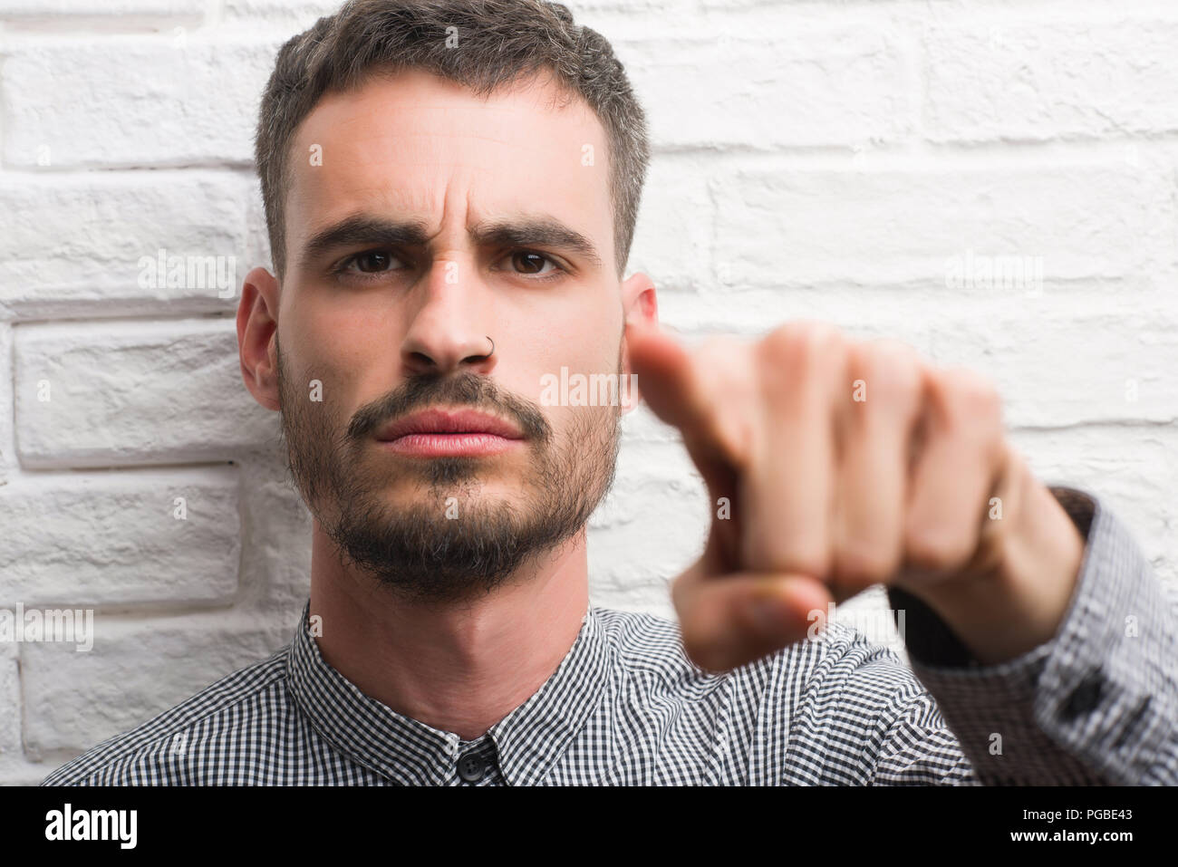 Young adult man standing over white brick wall pointing with finger to ...