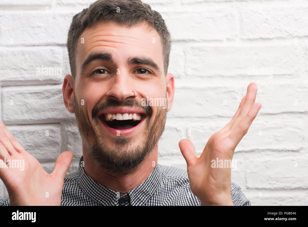 Young adult man standing over white brick wall very happy and excited ...