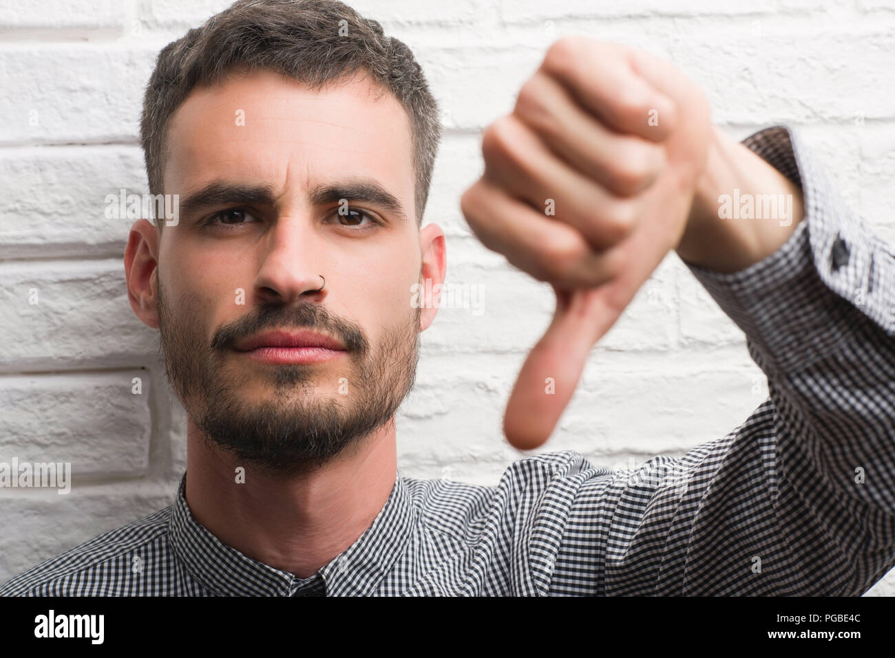 Young adult man standing over white brick wall with angry face ...