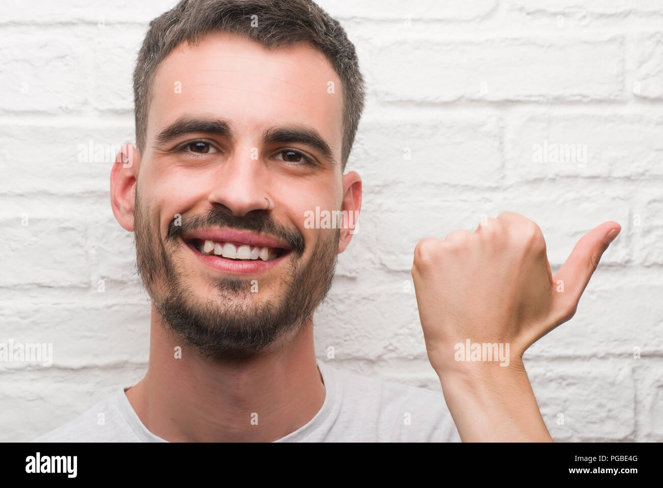 Young adult man standing over white brick wall pointing and showing ...