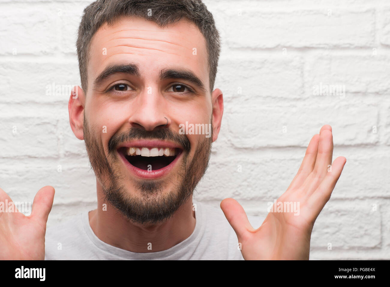 Young adult man standing over white brick wall very happy and excited ...