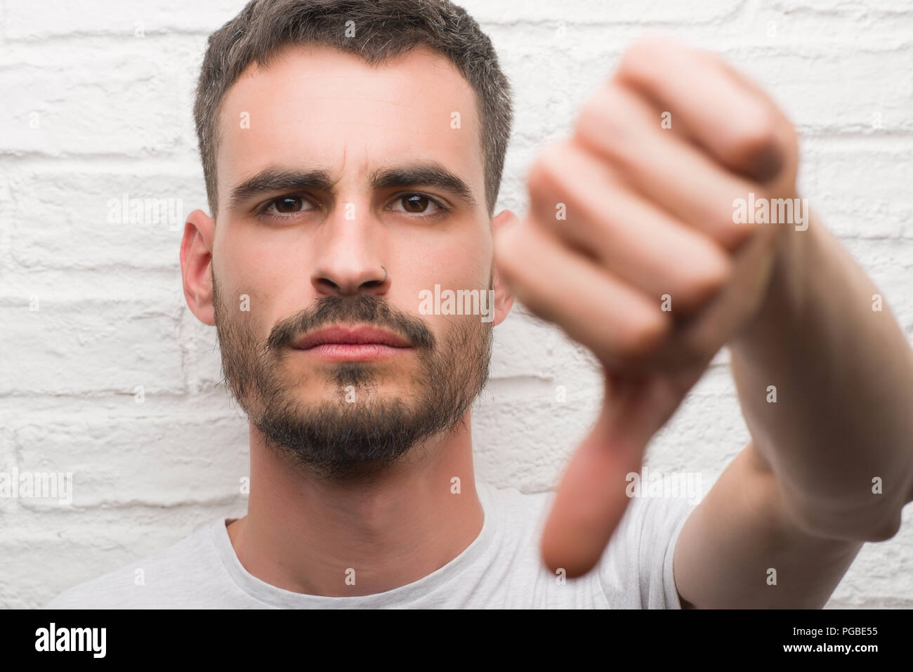 Young adult man standing over white brick wall with angry face ...