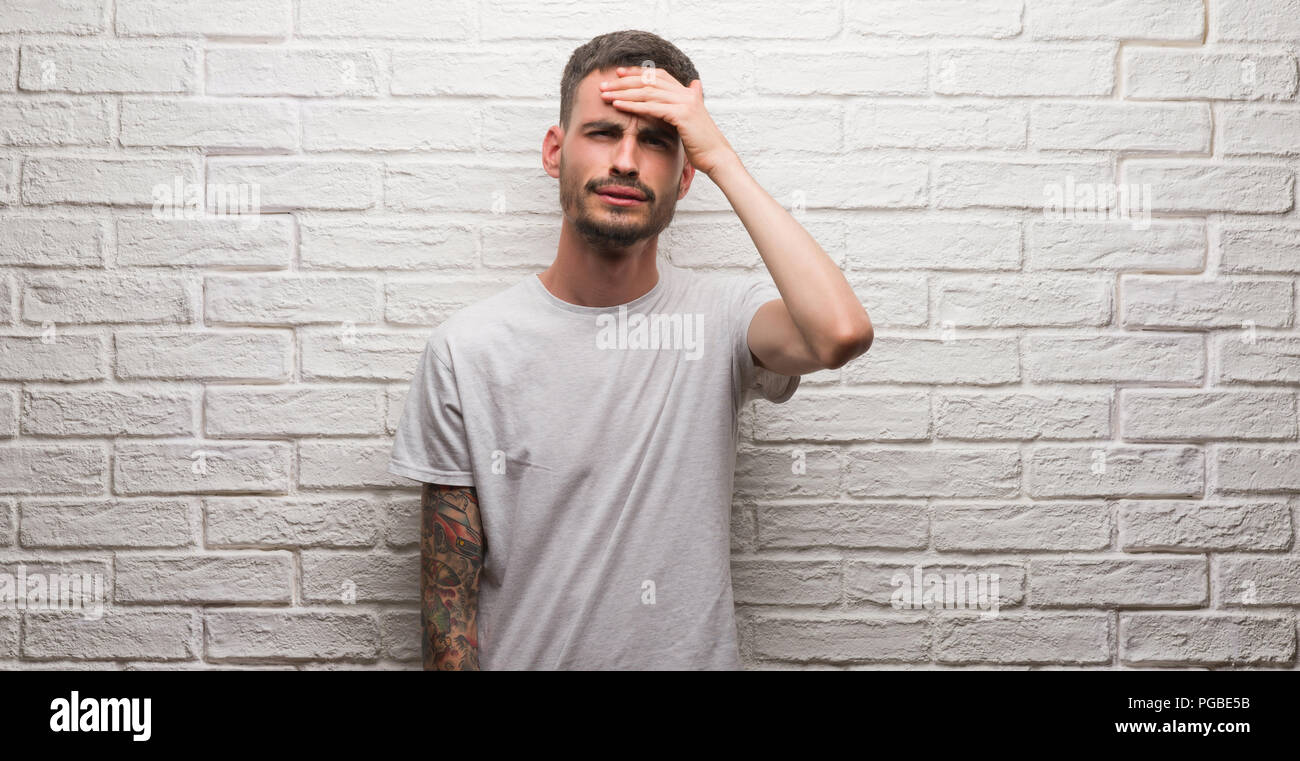 Young adult man standing over white brick wall stressed with hand on ...