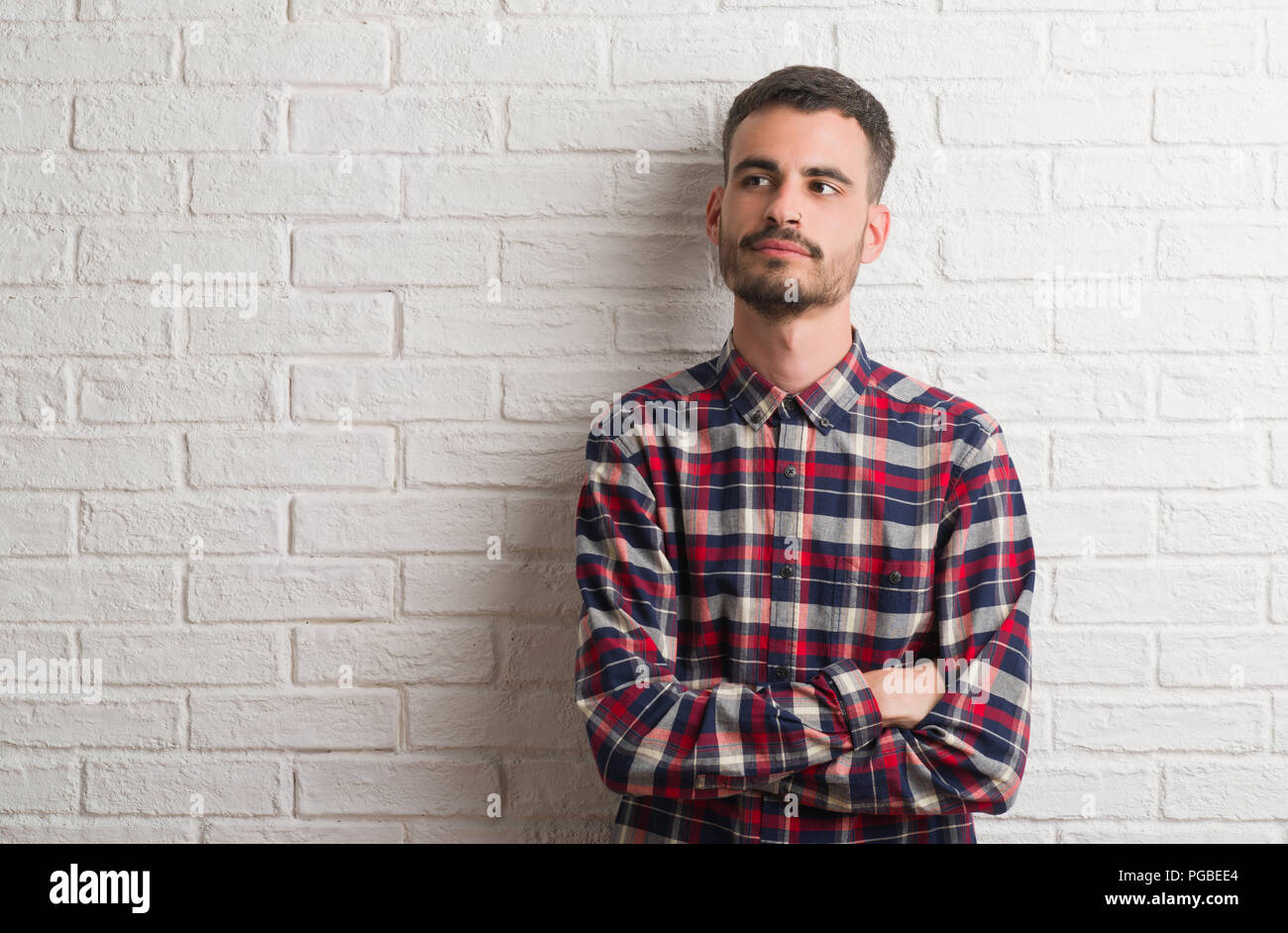Young adult man standing over white brick wall smiling looking side and ...