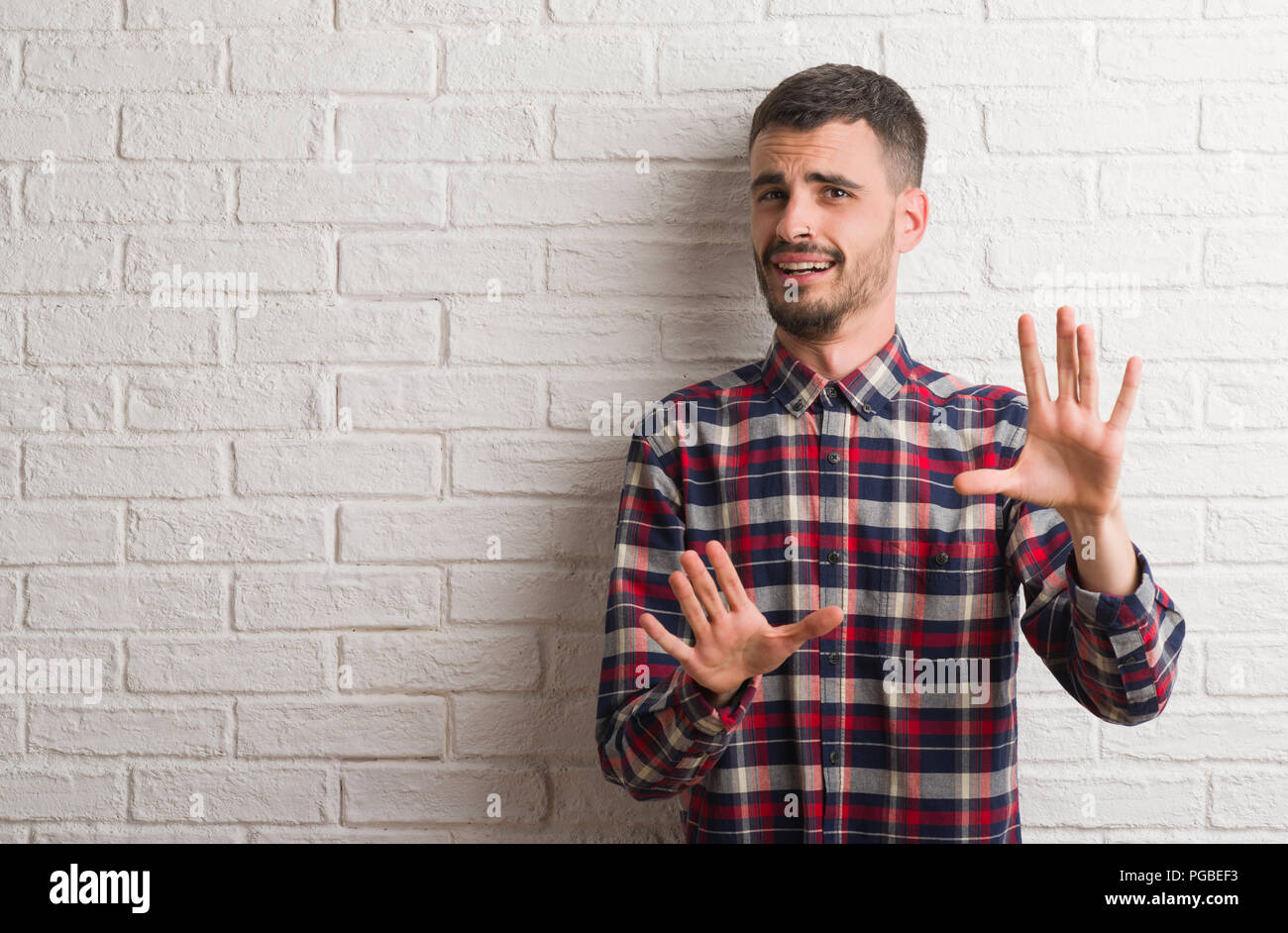 Young adult man standing over white brick wall afraid and terrified ...