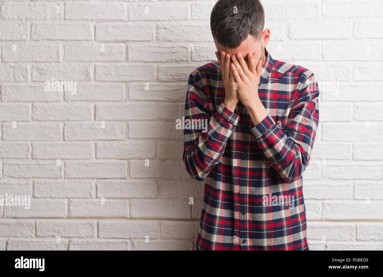 Young adult man standing over white brick wall with sad expression ...