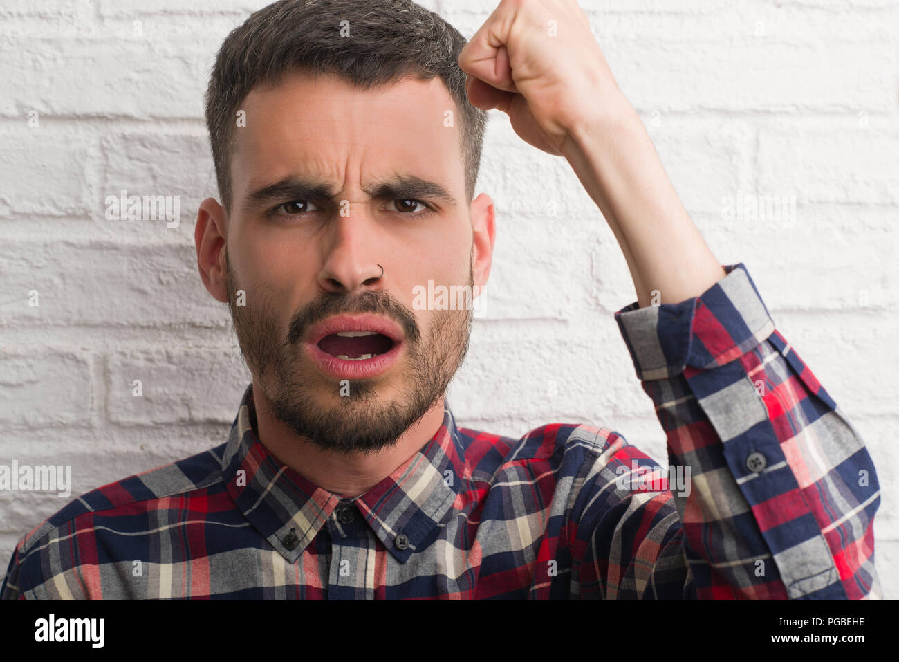 Young adult man standing over white brick wall annoyed and frustrated ...