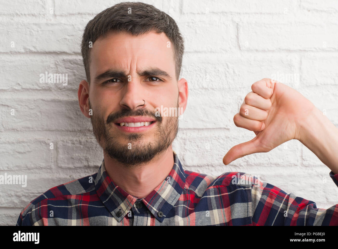 Young adult man standing over white brick wall with angry face ...