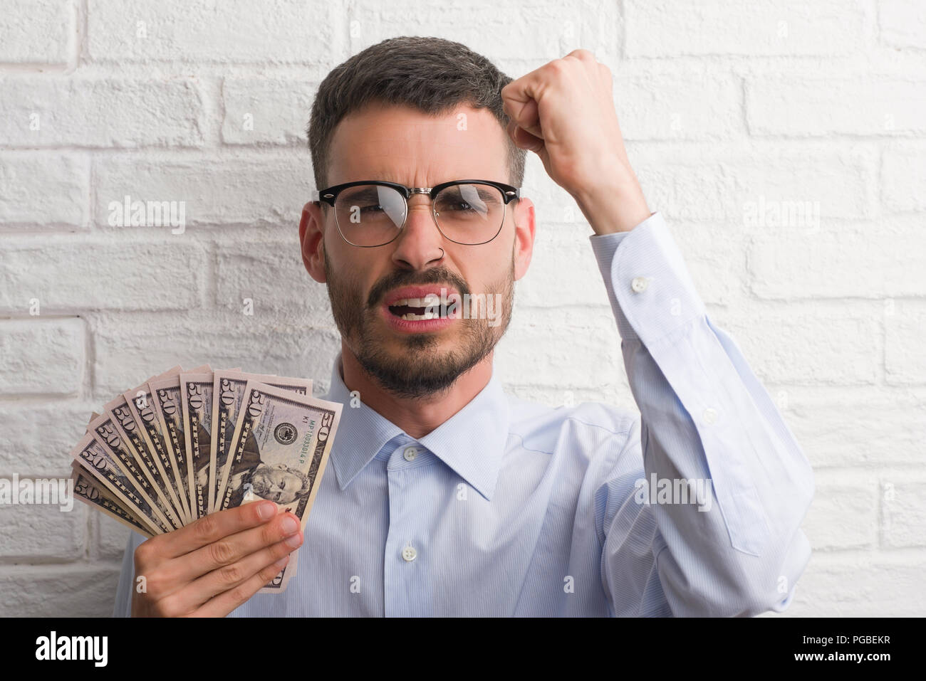 Young hipster business man holding dollars annoyed and frustrated ...