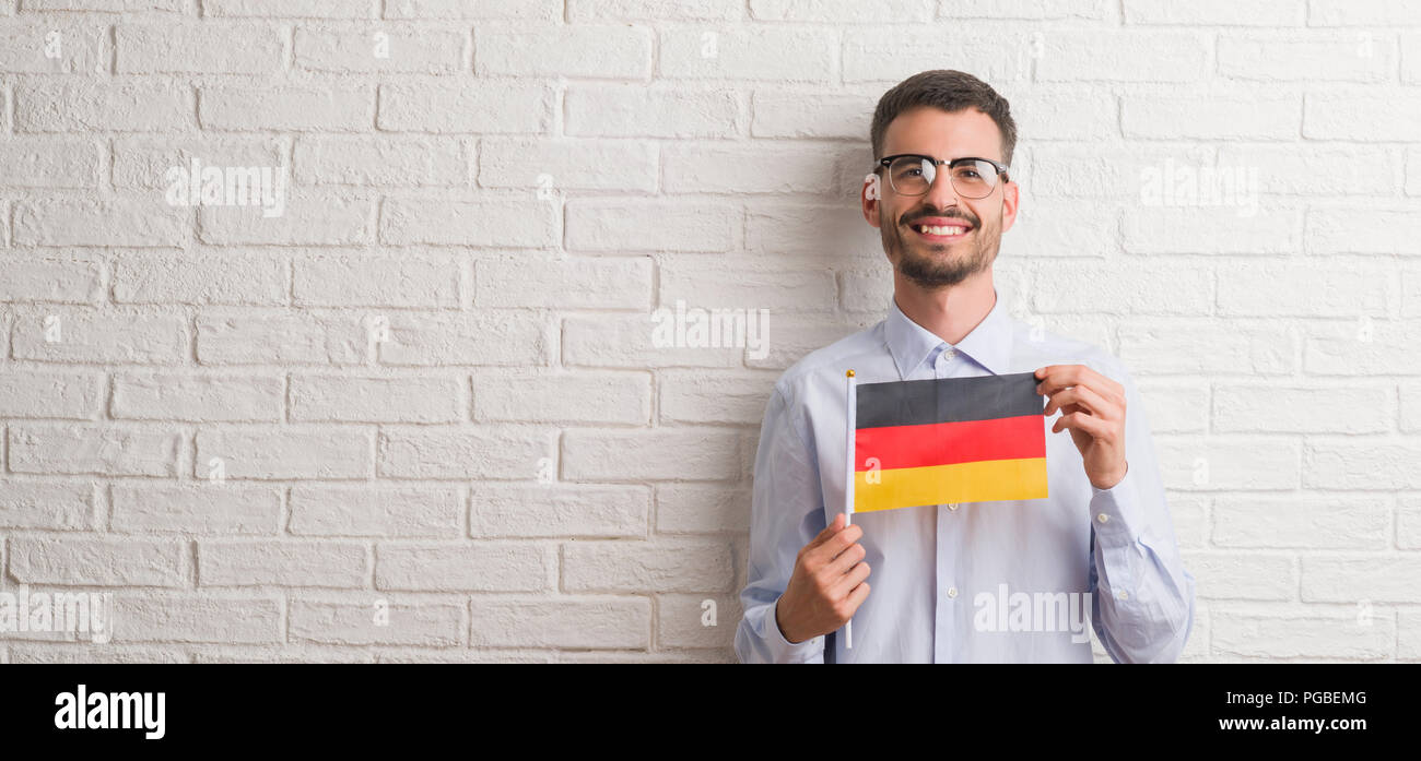 Young adult man over brick wall holding flag of Germany with a happy ...