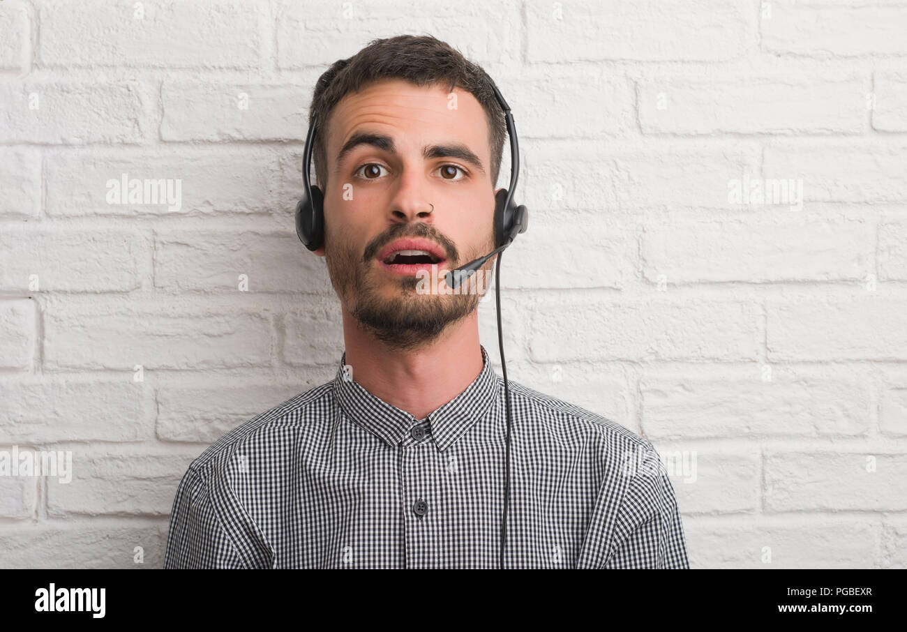 Young adult man over brick wall working as operator scared in shock ...
